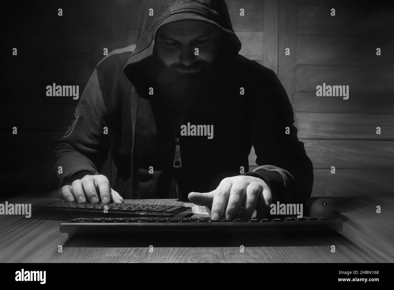 The hacker in the hood sits and works behind the computer Stock Photo ...