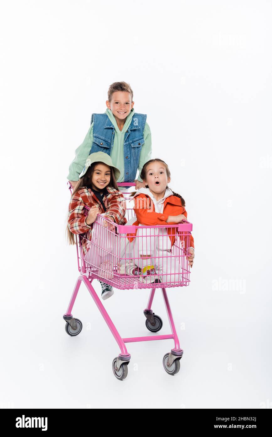 full length of happy boy standing behind girls in shopping cart ...