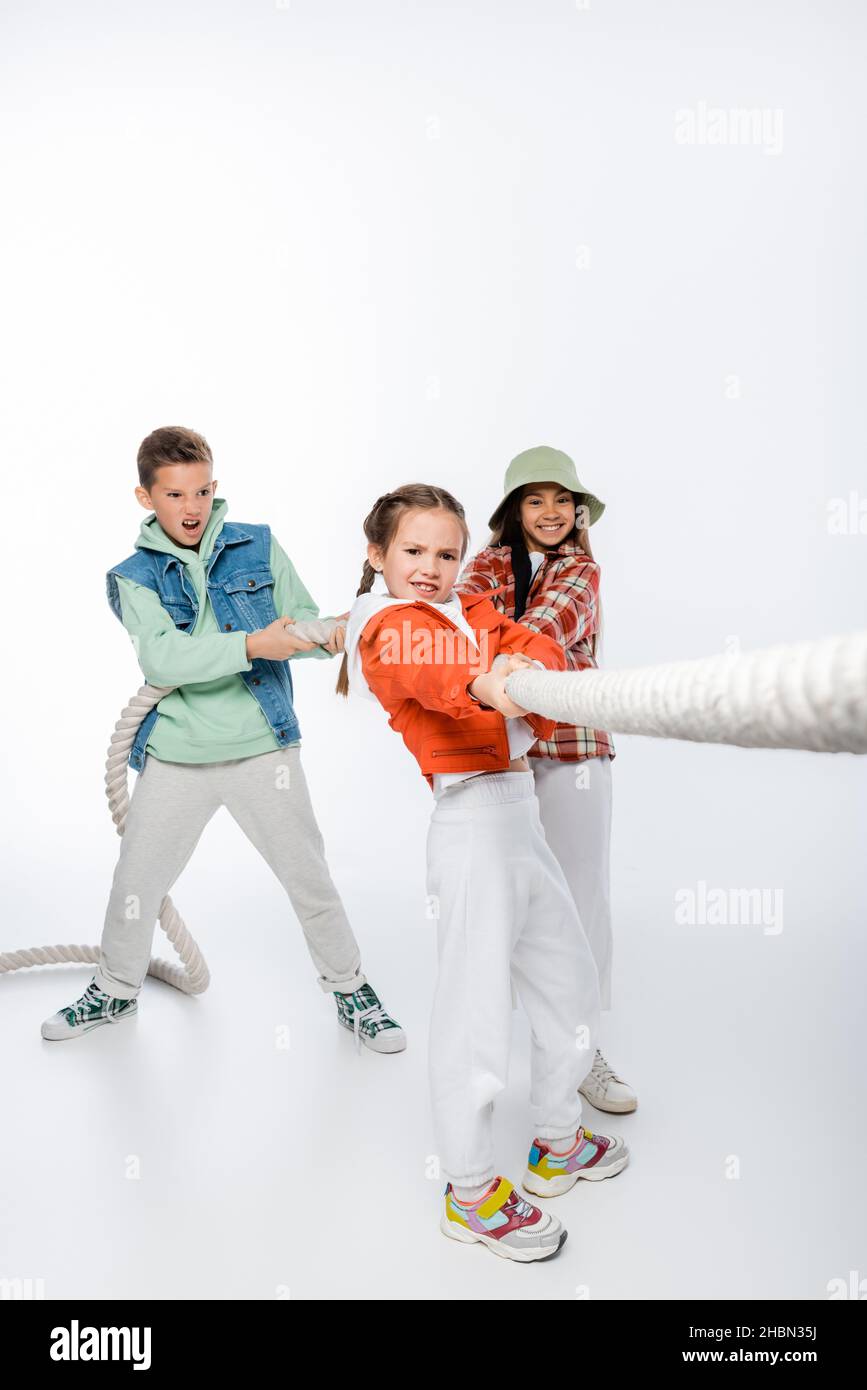 preteen children pulling rope while playing tug of war game on white ...