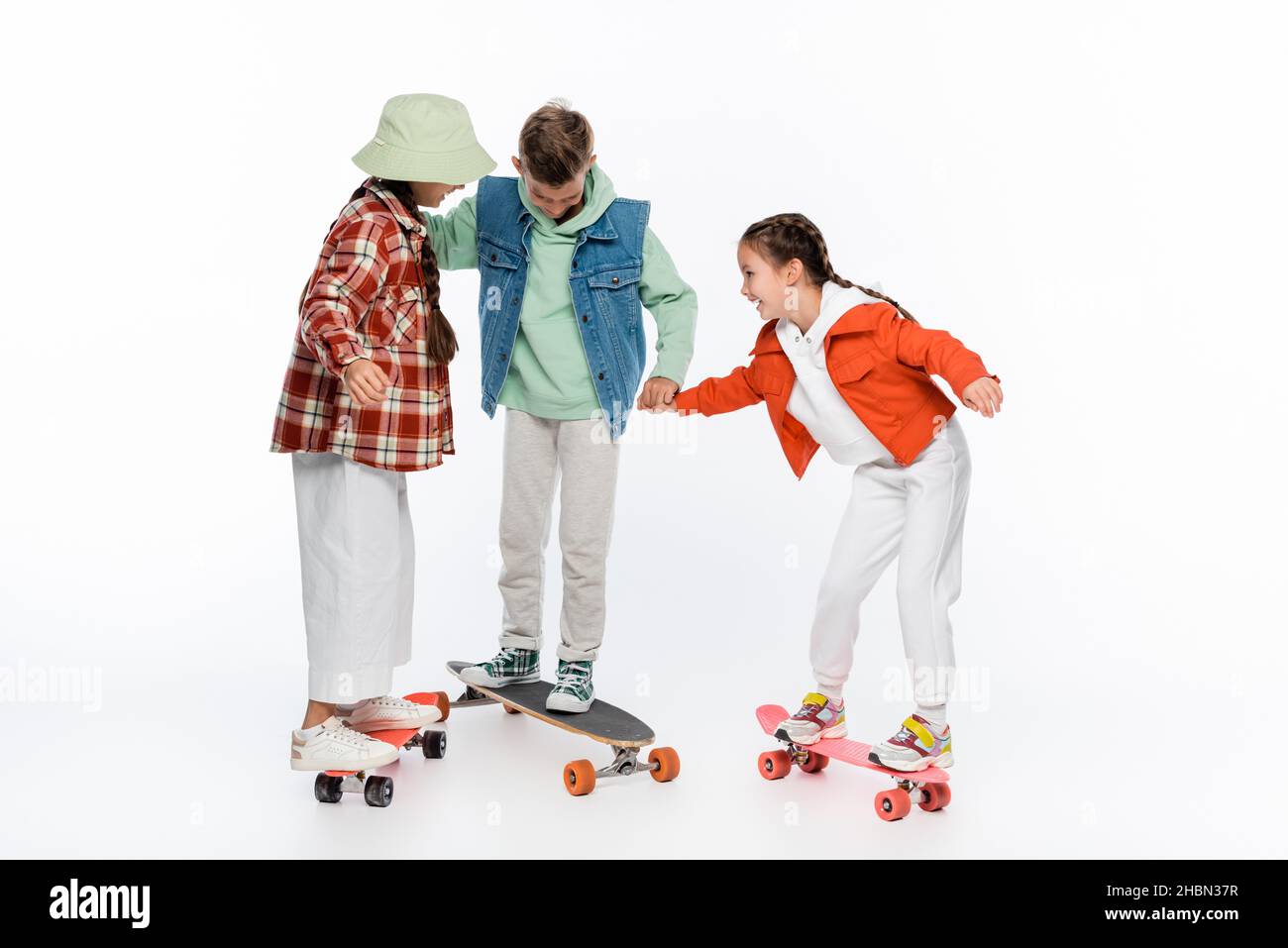 full length of trendy children smiling while riding longboard and penny ...