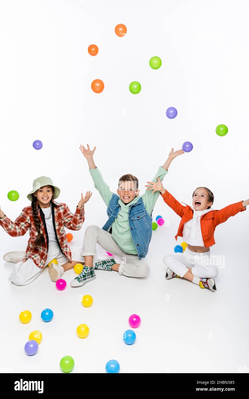 cheerful preteen kids sitting and throwing colorful balls in air on ...