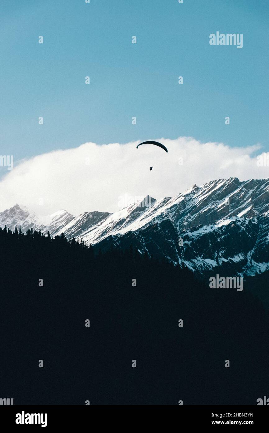 A vertical shot of a parachute floating above the snowy mountains and ...