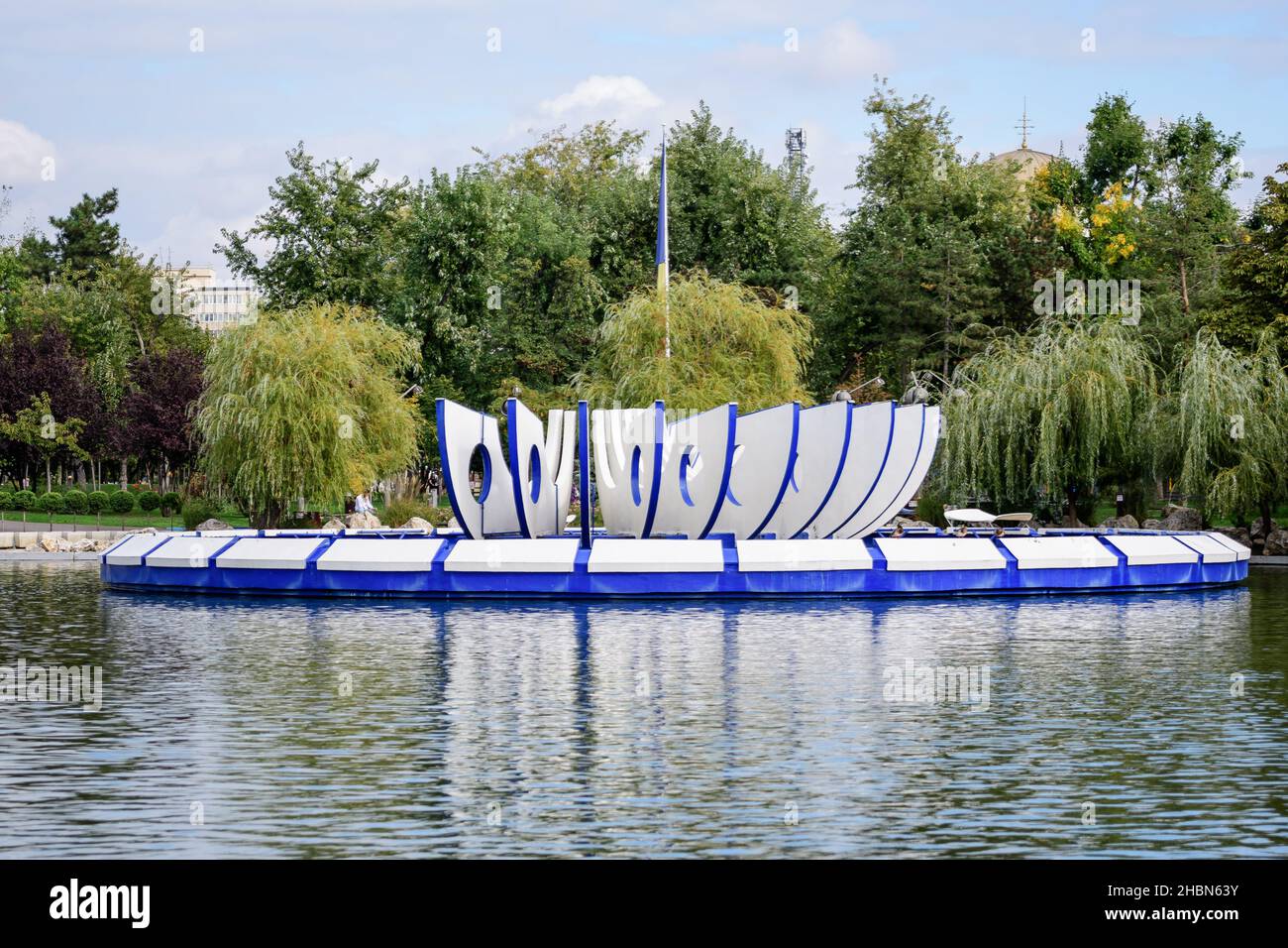 Landscape with white and blue fountain on the lake and green trees in ...