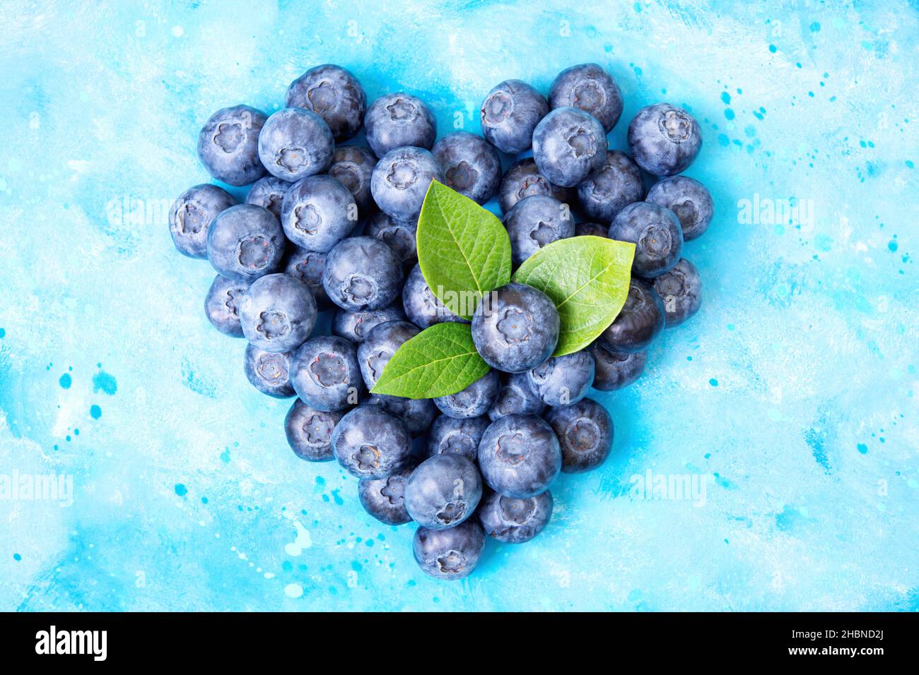 Heart symbol made from fresh ripe blueberries and green leaves on a ...
