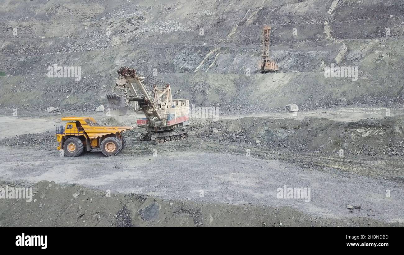 Excavator and dump truck while loading stone ore in a grey quarry ...