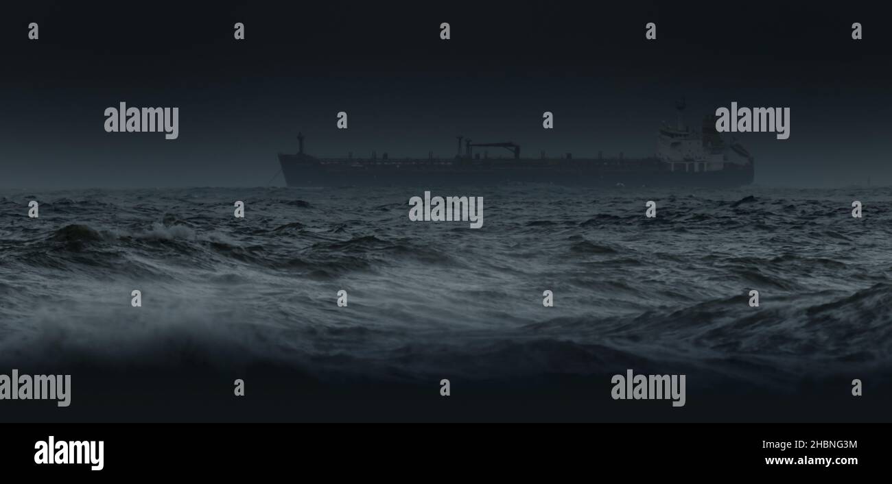A large cargo ship on the choppy sea waves against a dark sky late in ...