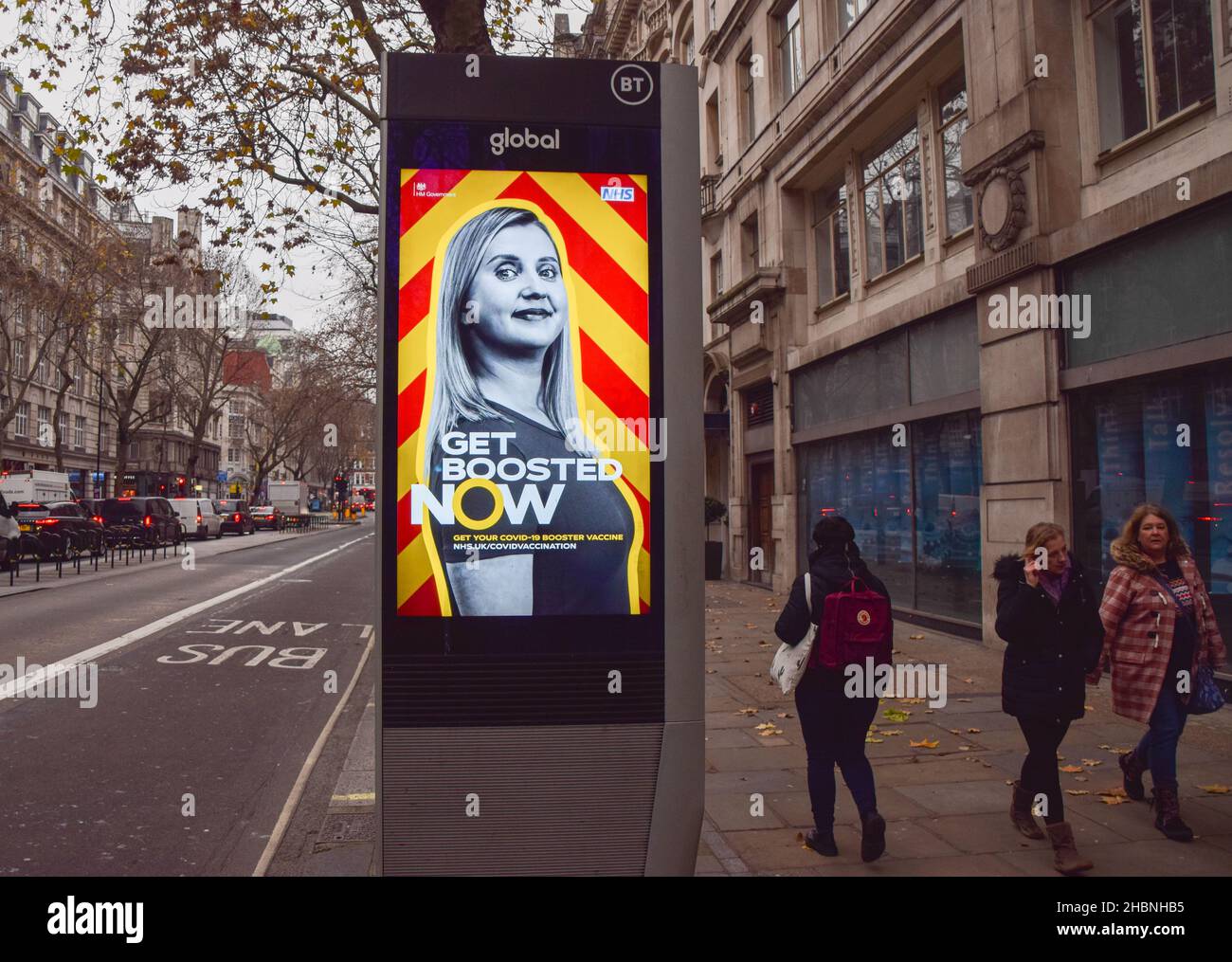 London, UK 18th December 2021. People walk past an electronic display ...