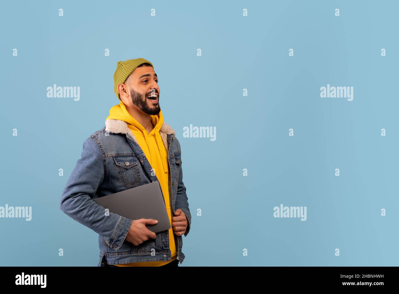 Young arab guy holding laptop and looking aside at free space, arabic ...