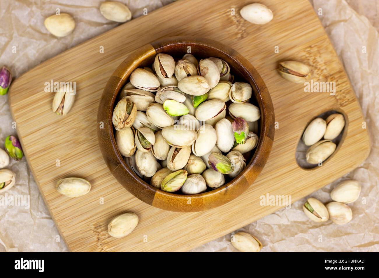 Top view of roasted salted pistachio nuts in nutshell in wooden bowl on textured background ...
