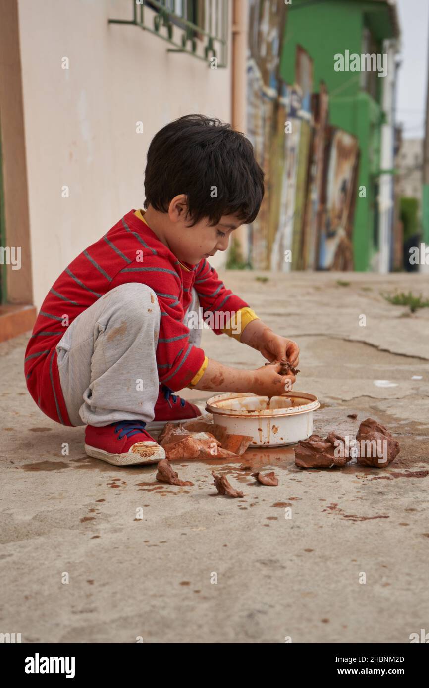 Boy kneeling with red shirt makes figures with clay Stock Photo - Alamy