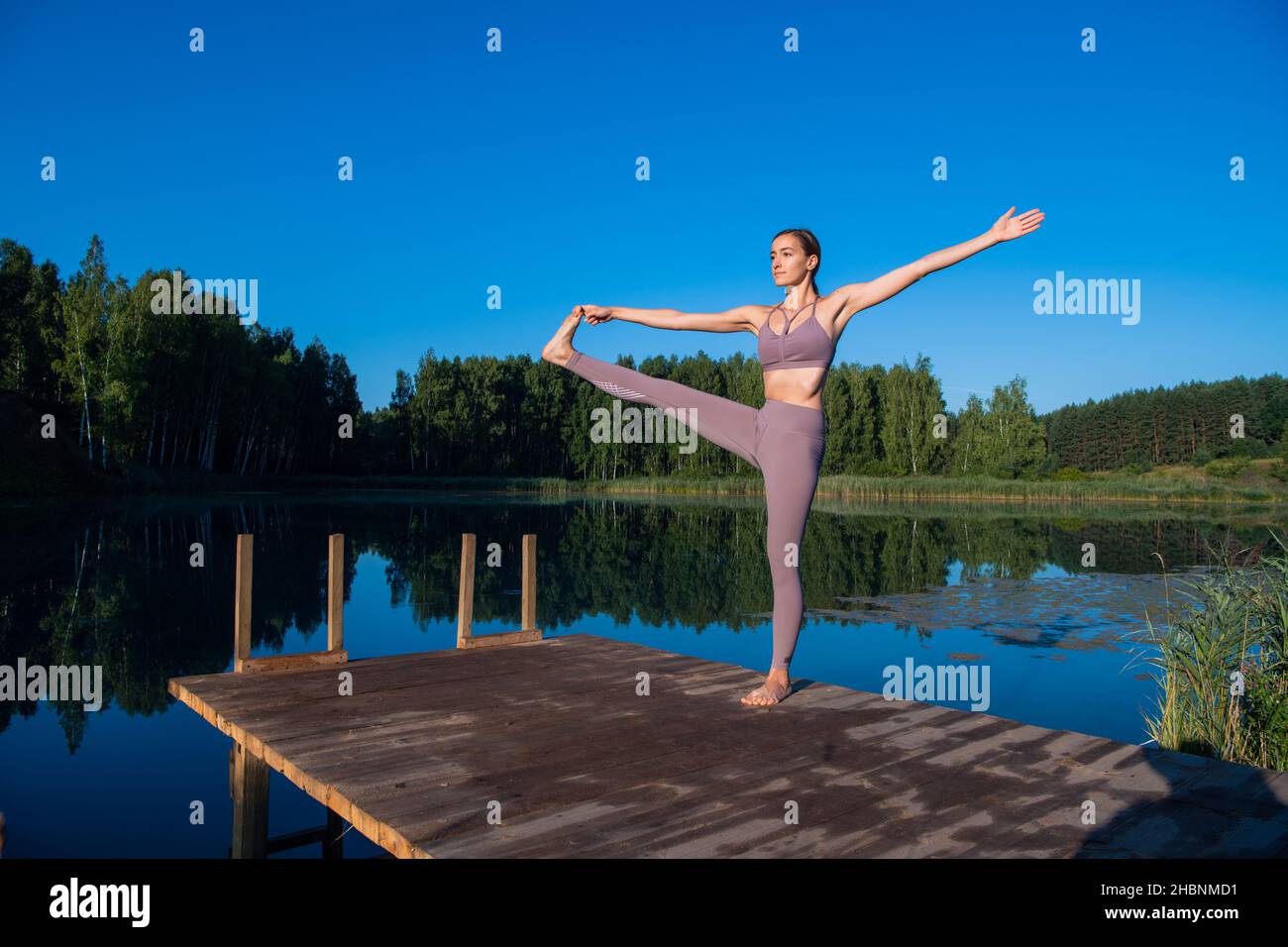 Young Woman practicing yoga on the wooden berth at lake. Single sport ...