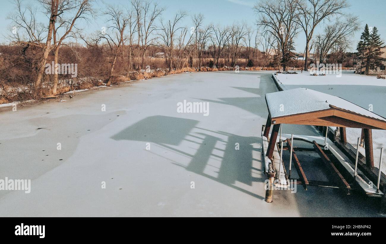 View over a frozen river lined by trees and shadow of a boat lift ...