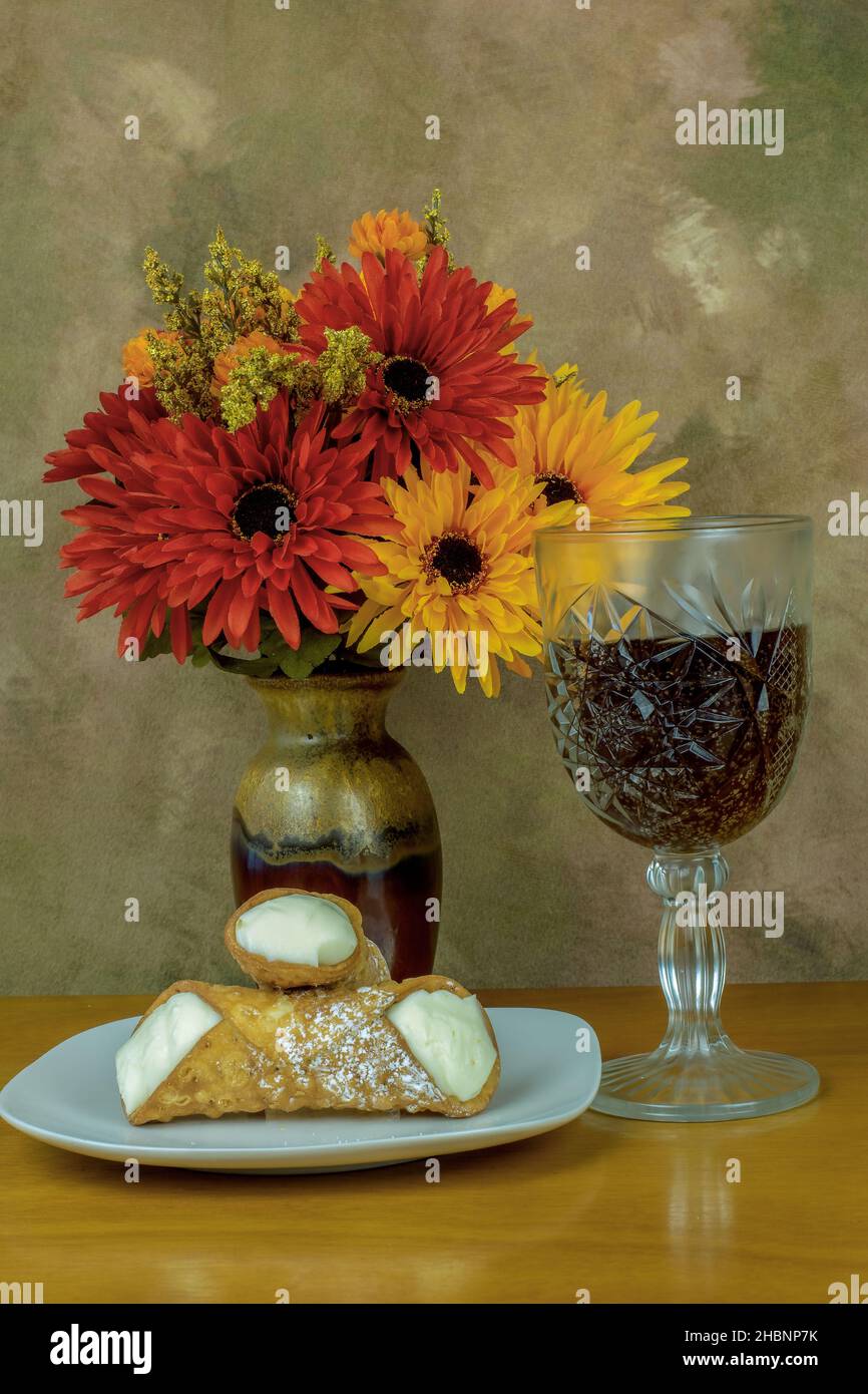 two cream fill cannolis with assorted flowers and wine in the back ...