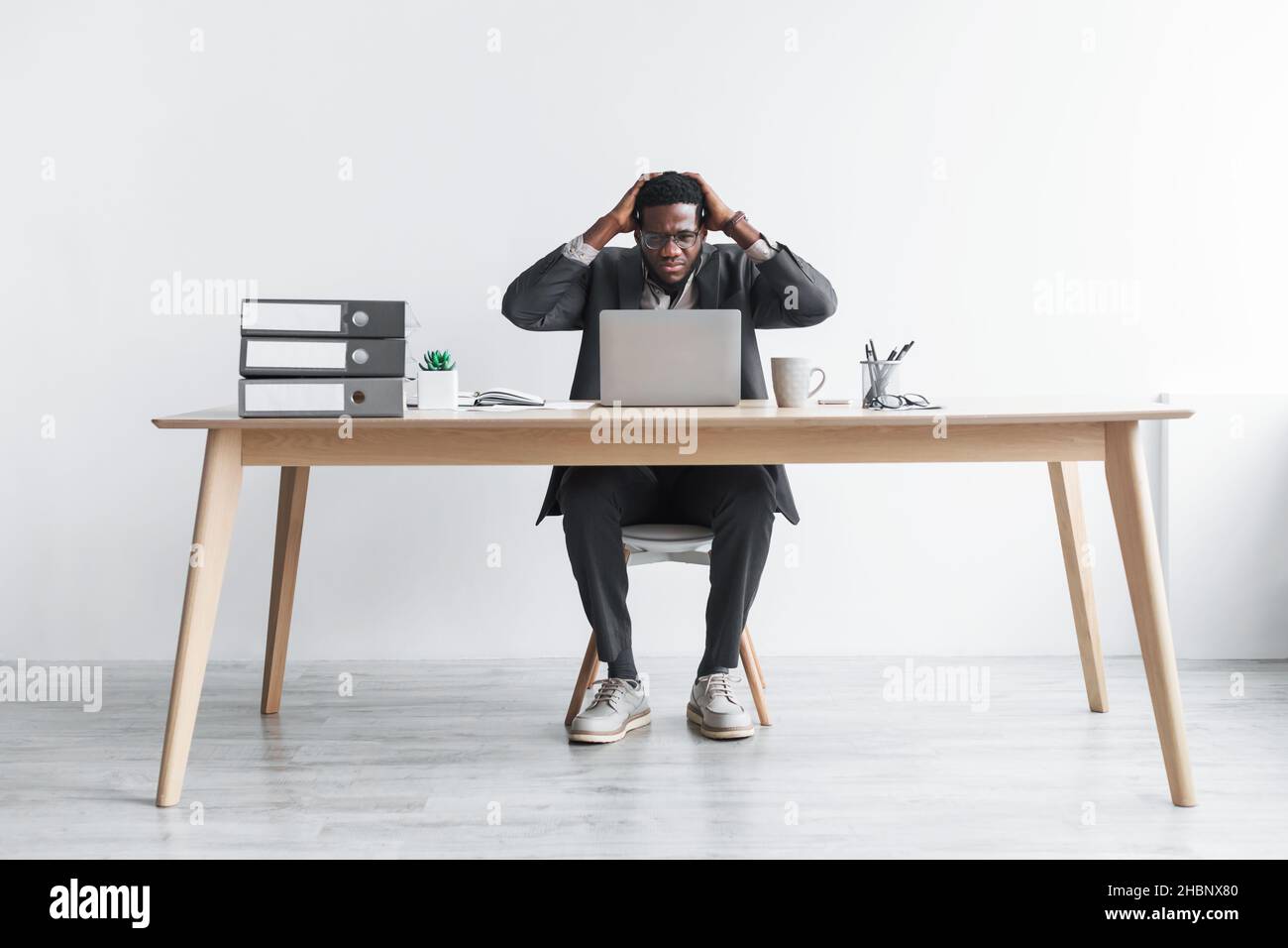 Stressed young black man using laptop, sitting at desk, grabbing his ...