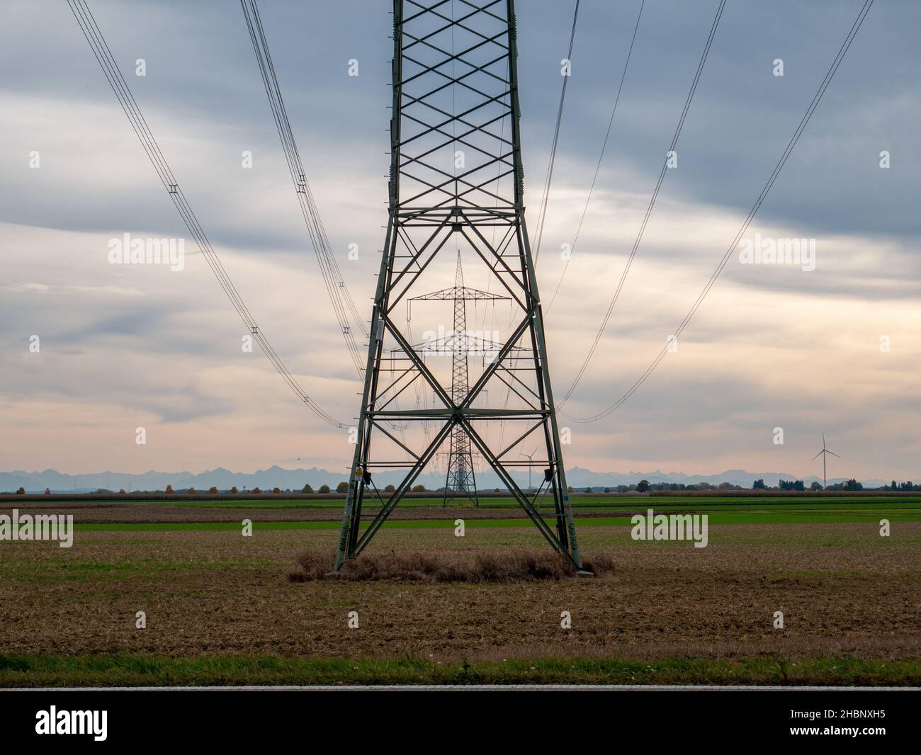 A transmitter tower with high voltage cables in a field on a cloudy day ...