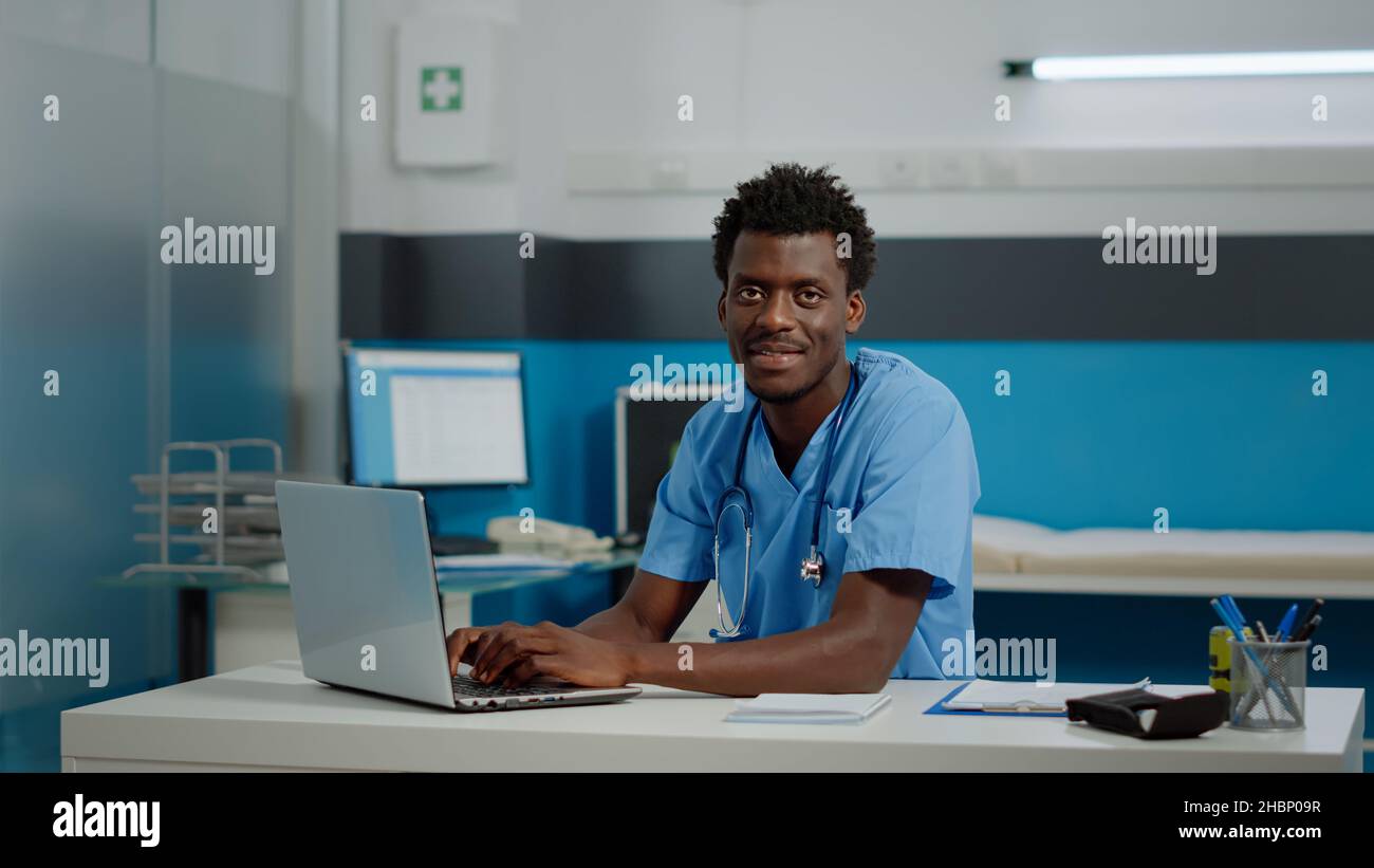 Portrait of male nurse with uniform and stethoscope using laptop on ...