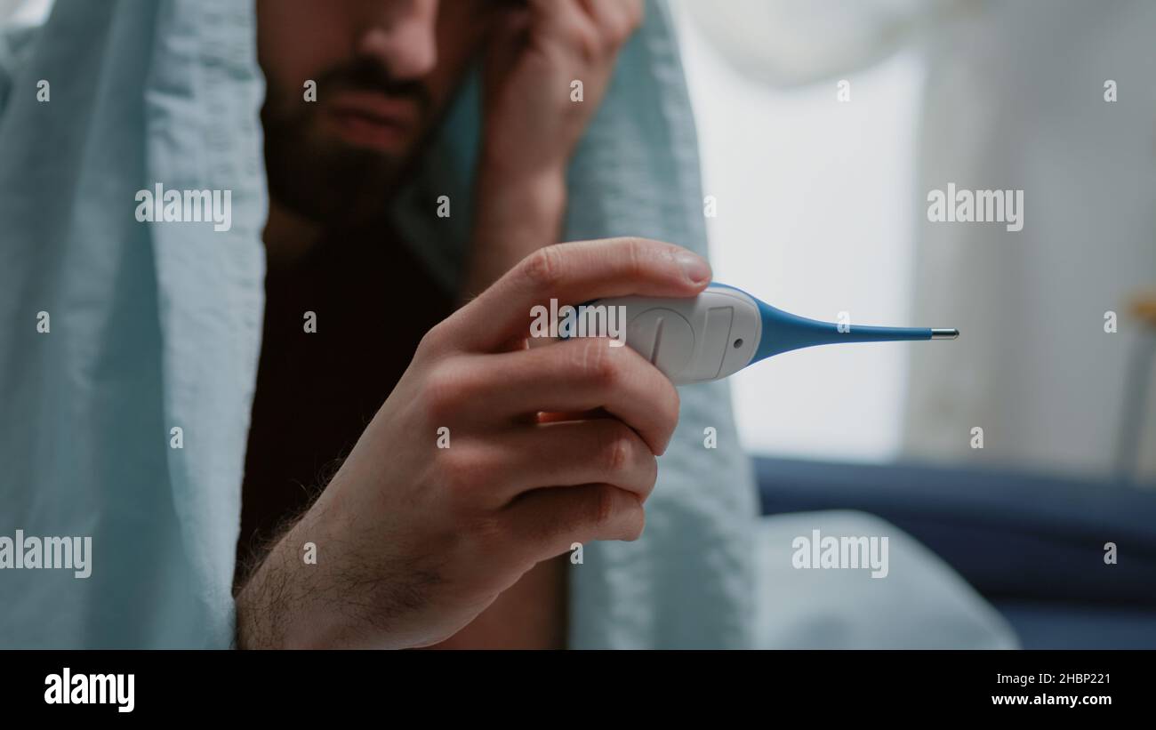 Close up of sick man looking at thermometer measuring fever and flu ...