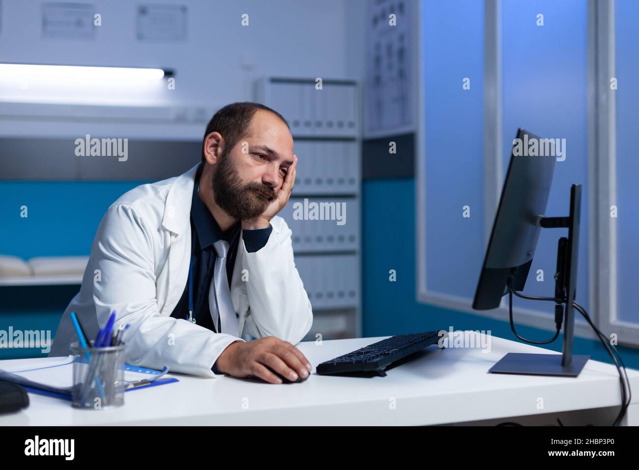 Sleepy doctor working late at night with computer for medical checkup ...