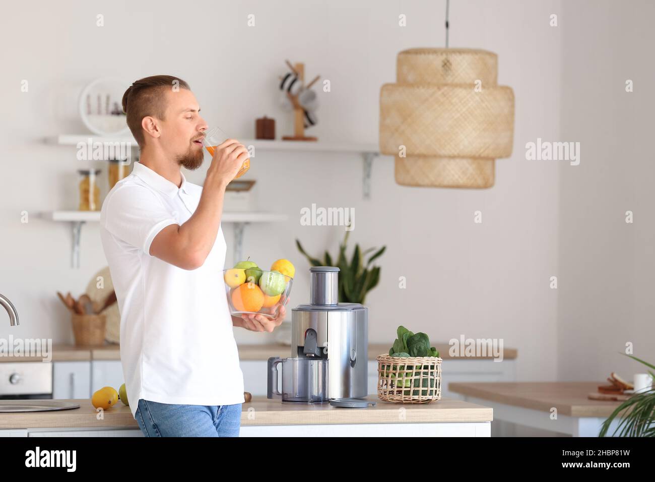 Young man with glass of fresh fruit juice near modern juicer in kitchen ...