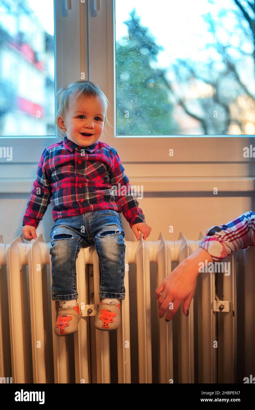 Cute little boy sitting on a radiator against the window Stock Photo ...