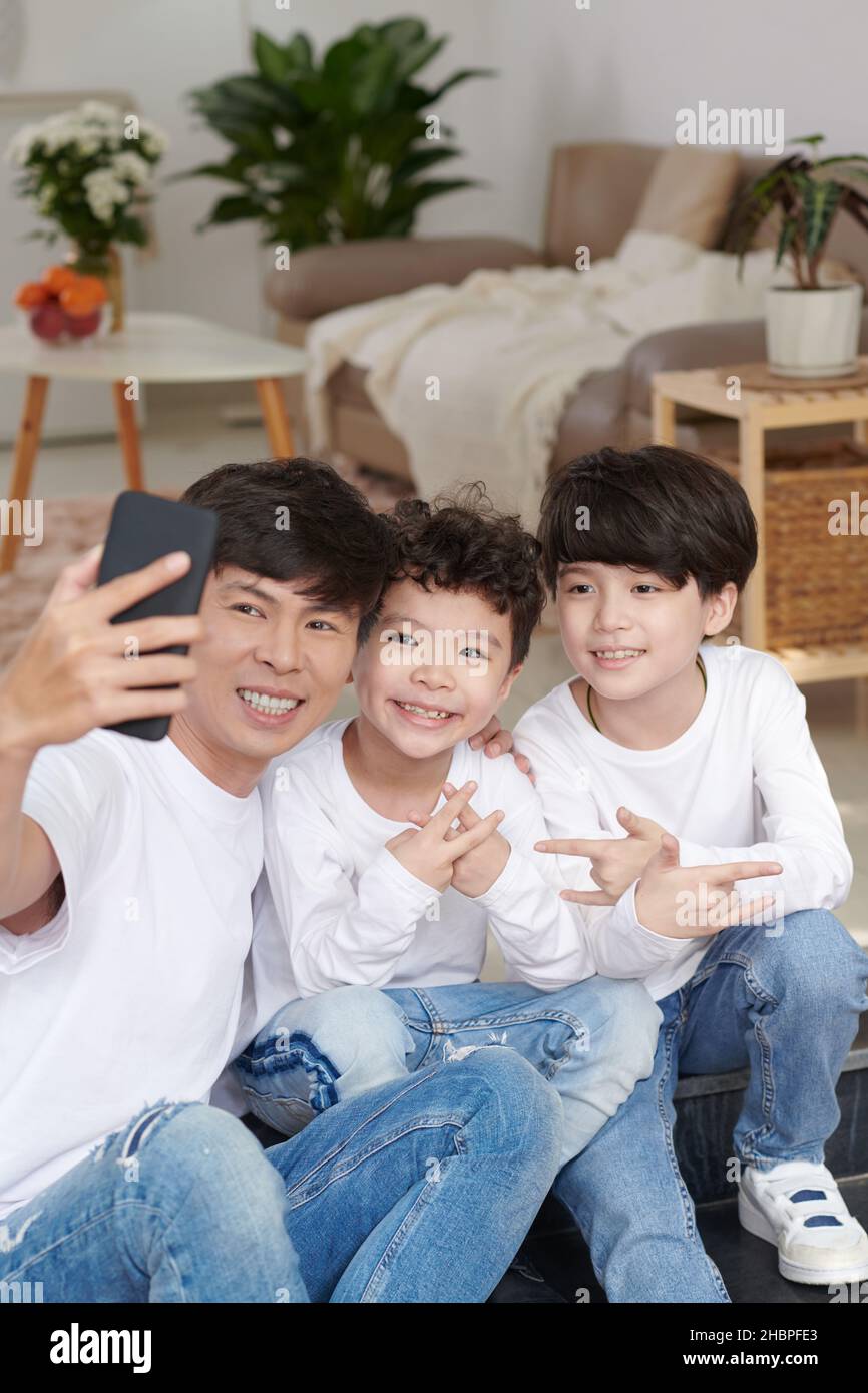 Joyful father taking selfie with two kids at home to post on social ...