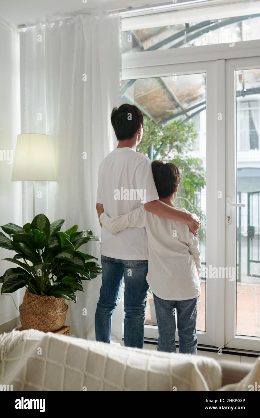 Man embracing his son when they are looking through house window, self ...