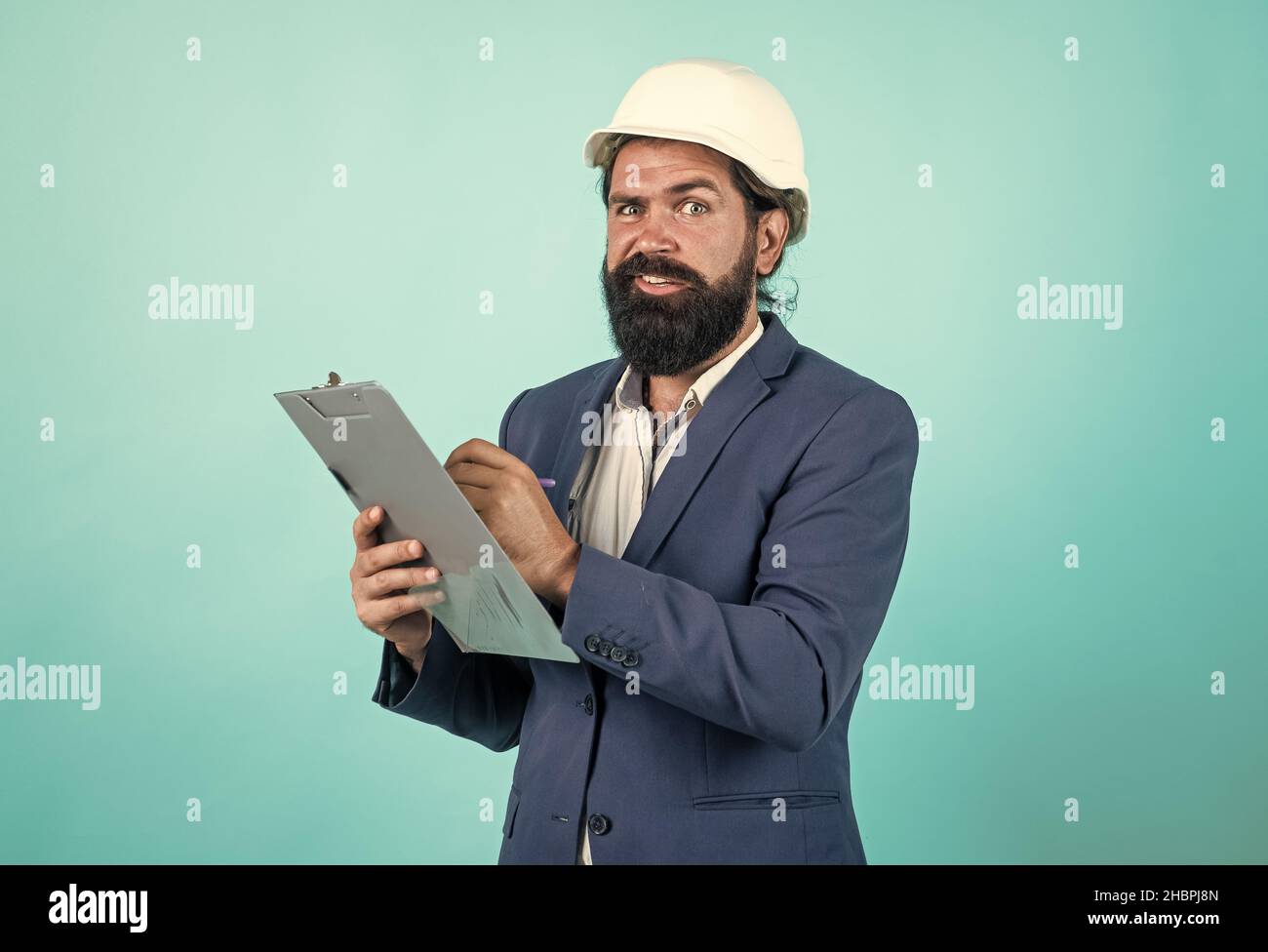 serious foreman in helmet and suit writing in paper folder, making ...