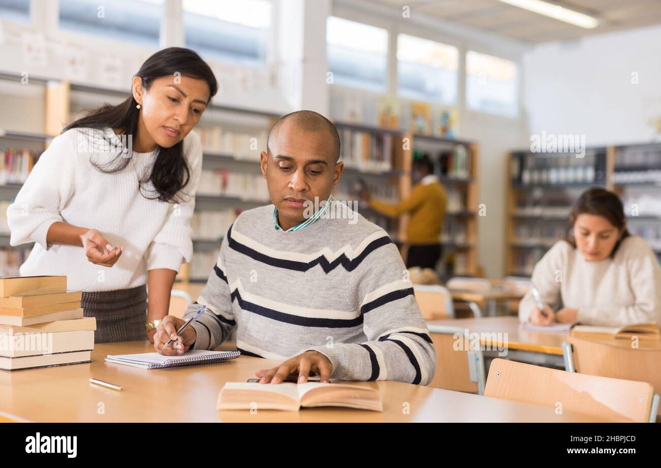 Young adult people studying together in library, talking, reading books ...