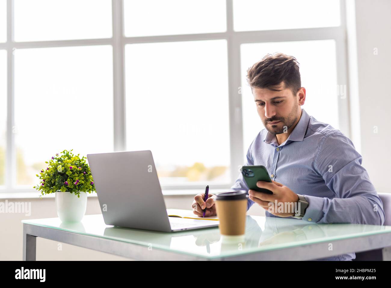 Multi-tasking young businessman working in the office while reading an e-mail on laptop and ...