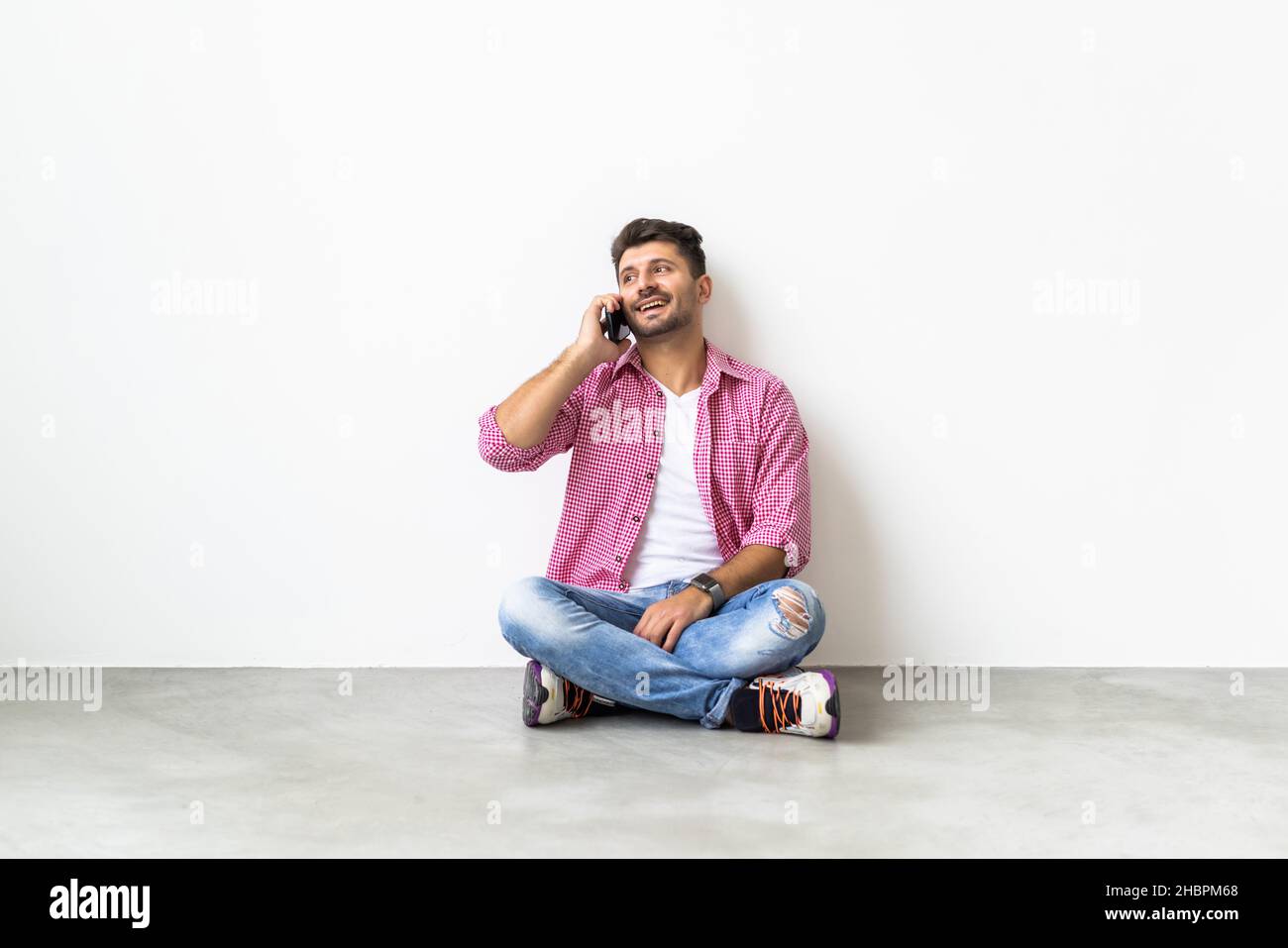 Young man talking on a phone while sitting on the floor and leaning ...