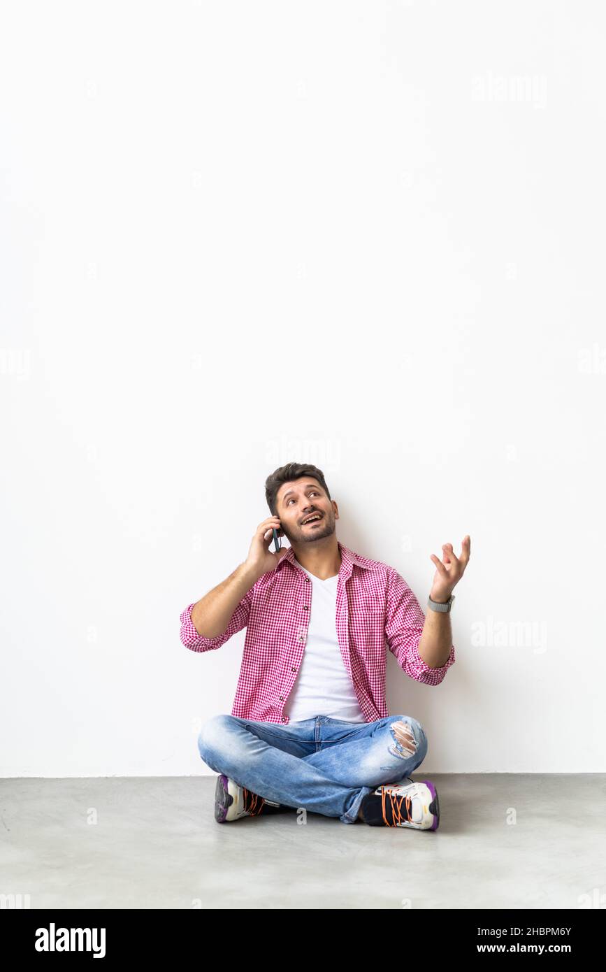 Young man talking on a phone while sitting on the floor and leaning ...
