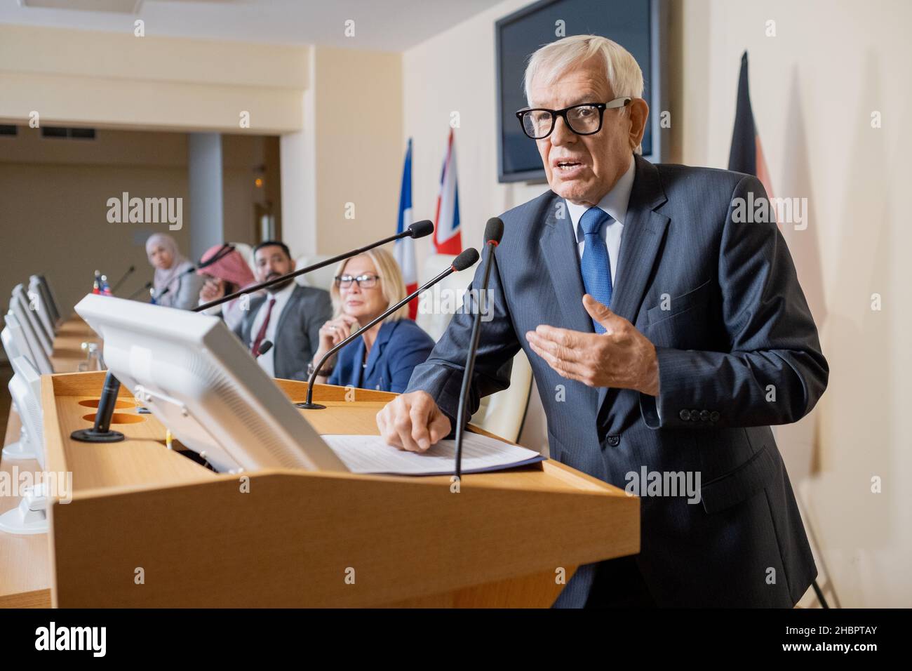 Confident mature delegate speaking by tribune while standing in front ...