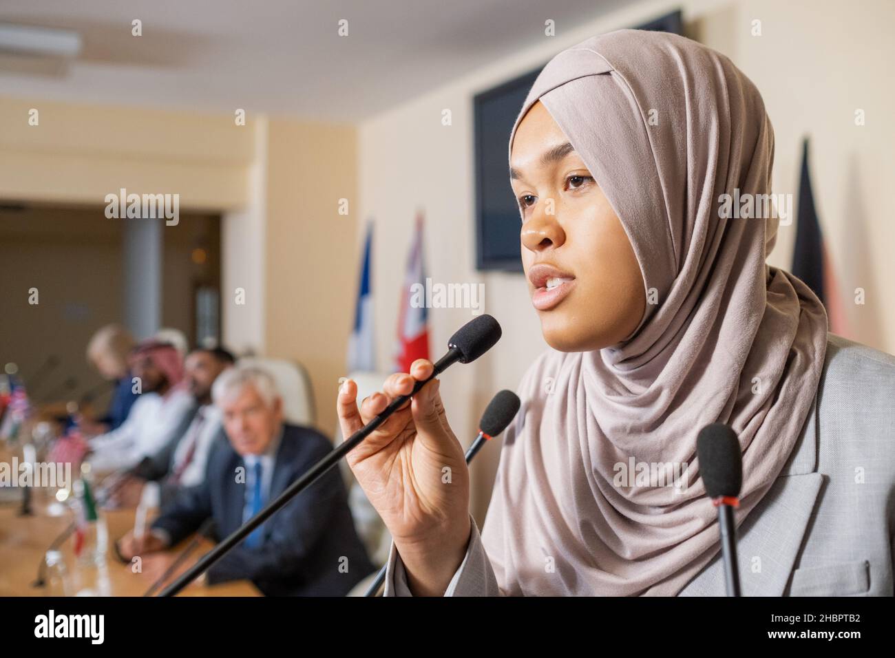 Pretty young Muslim woman in hijab speaking in microphone while ...