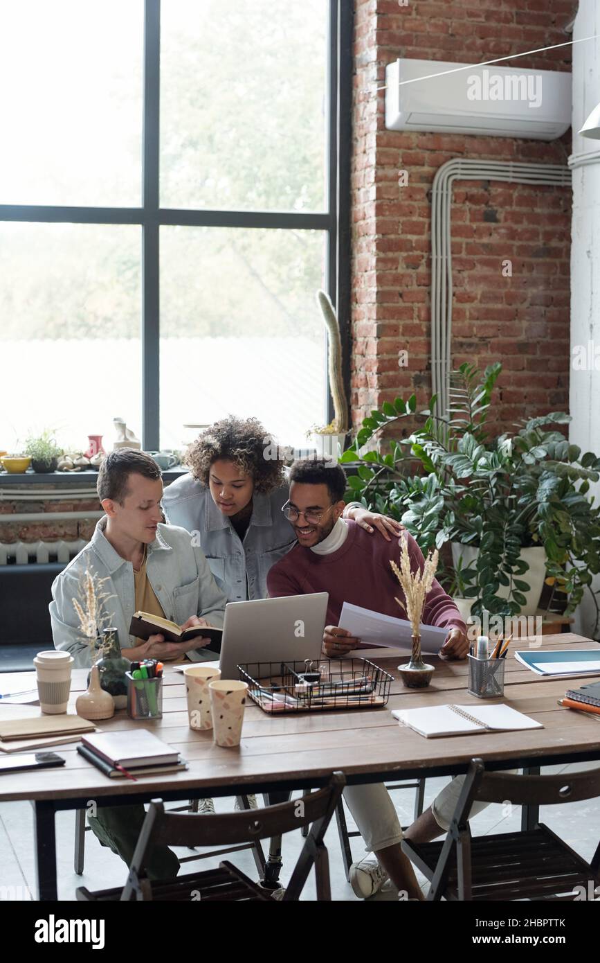 Three intercultural co-workers looking at laptop display while ...