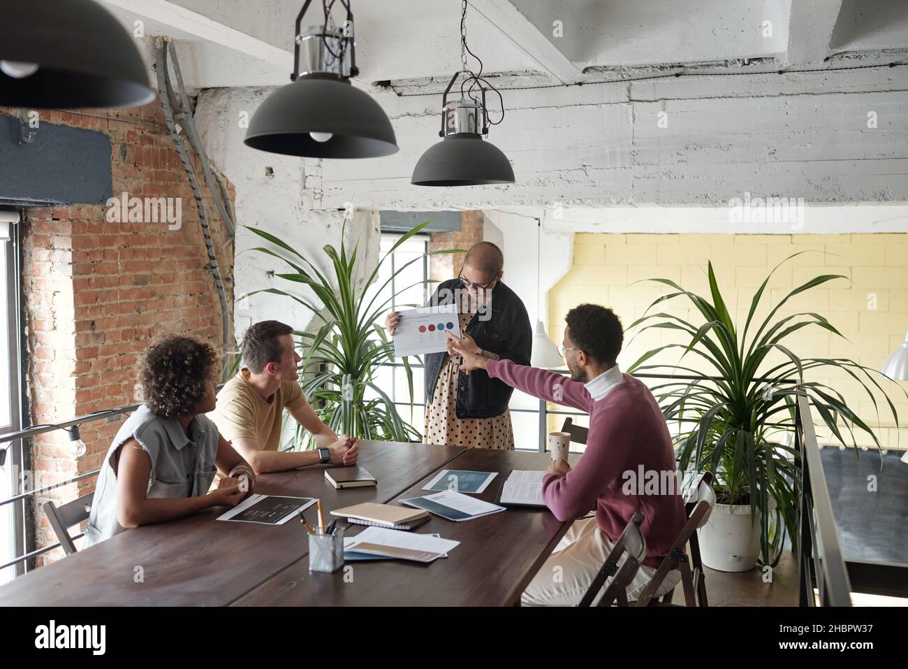 Young female economist showing paper with financial data to colleagues ...
