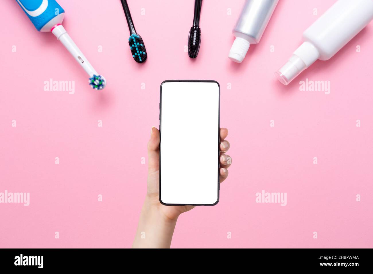 Hand with a smartphone and various toothbrushes, toothpaste and mouth ...
