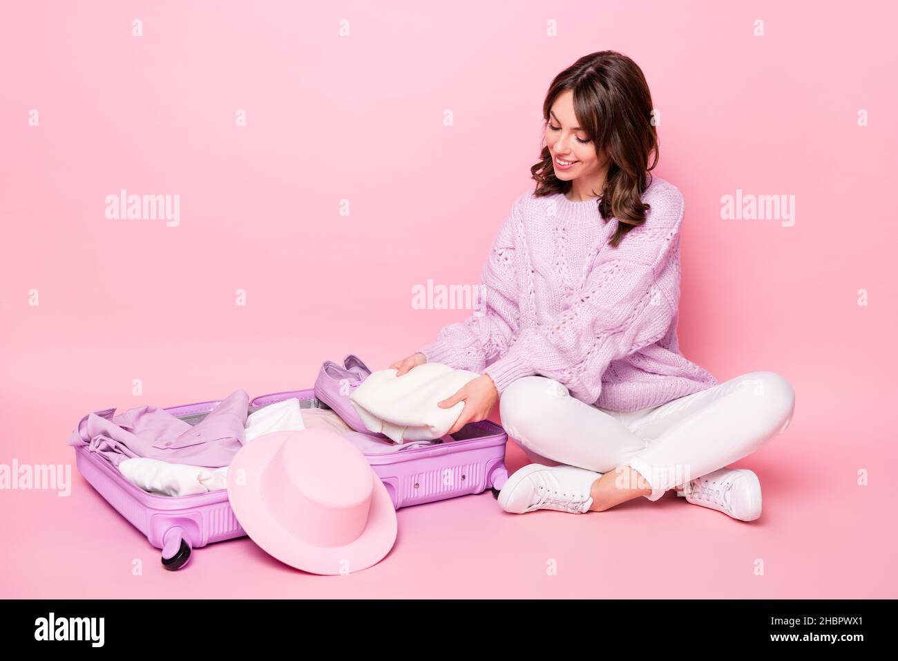 Portrait of pretty cheerful girl packing things bag folding clothes ...