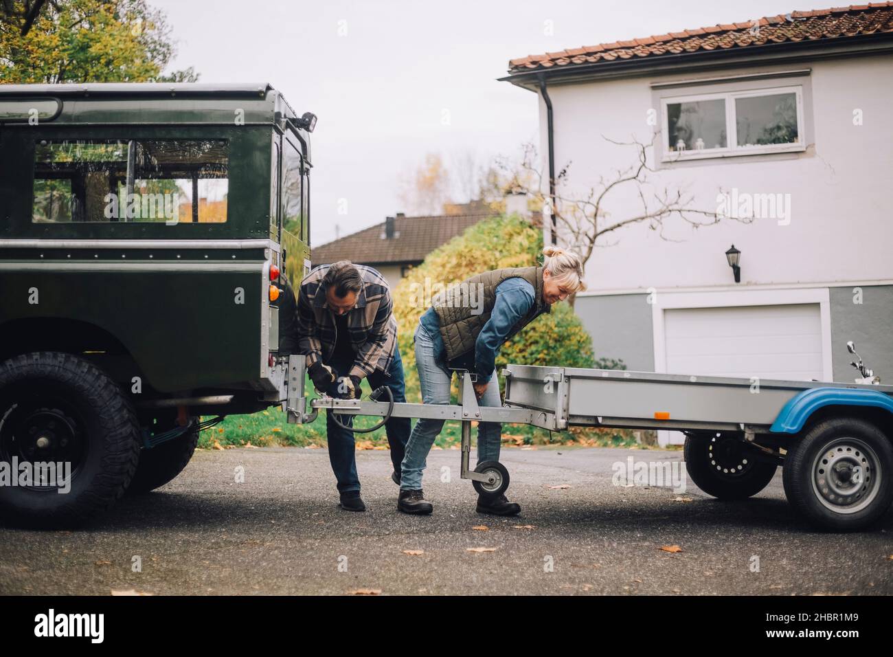 Male and female friends towing trailer to sports utility vehicle at ...