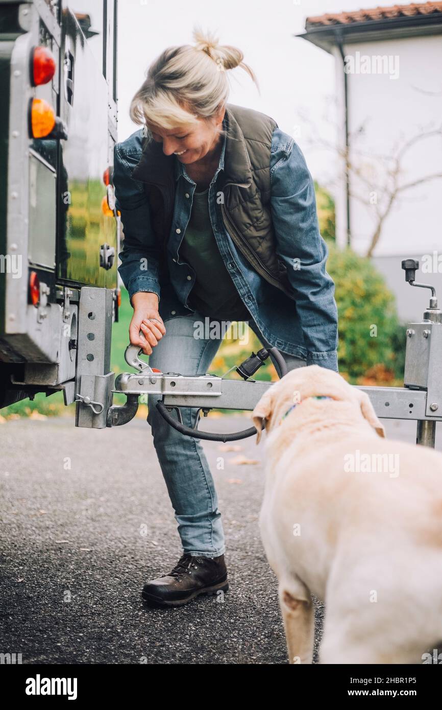 Smiling woman towing trailer to sports utility vehicle by dog on ...