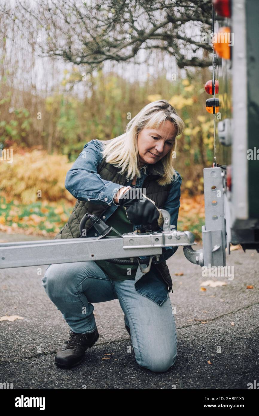 Mature woman fastening trailer to sports utility vehicle on driveway ...