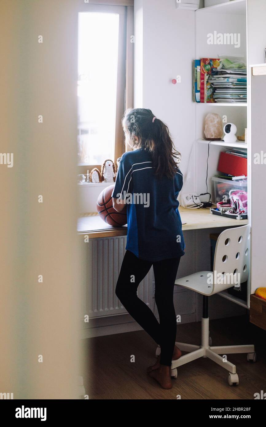 Rear view of girl looking through window at home Stock Photo - Alamy