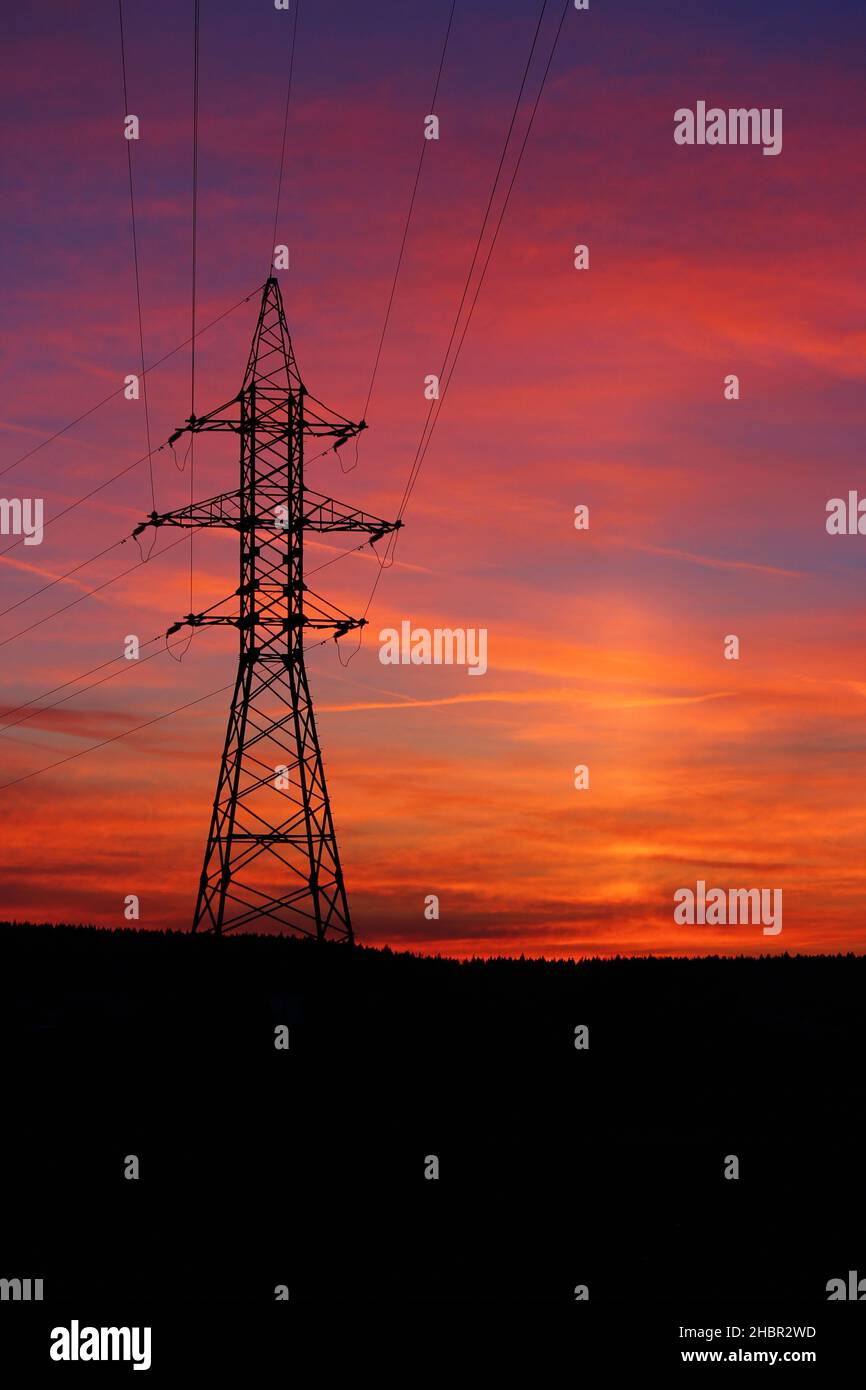 Colorful fiery red sunset and solar pillar effect. View of power lines ...