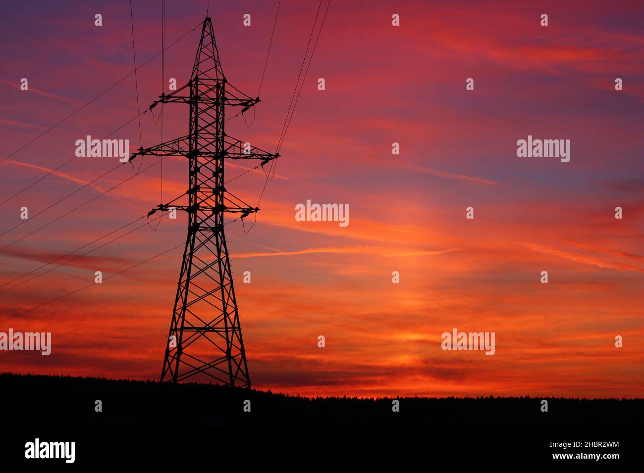 Colorful fiery red sunset and solar pillar effect. View of power lines ...