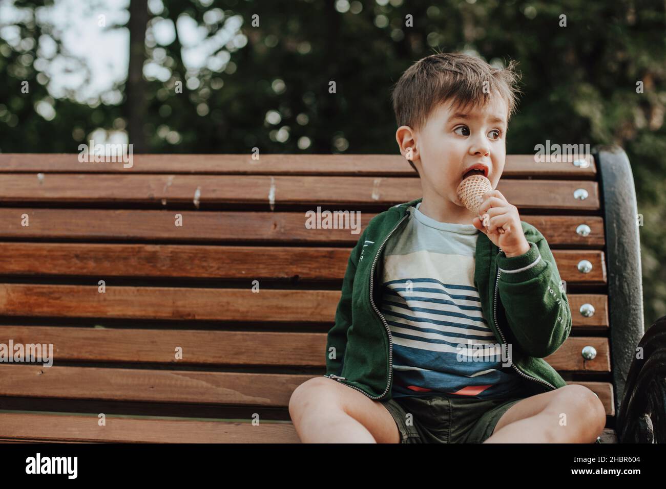 Front view of a caucasian boy eating ice cream sitting on a bench in ...