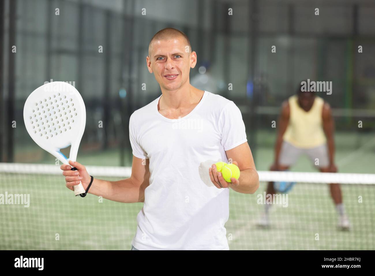 Portrait of positive man with racket and ball in his hands on the padel ...