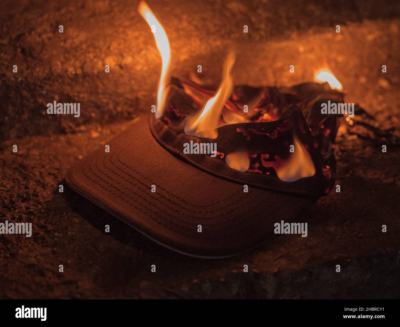A dark textile cap burns with bright fire while lying on a concrete ...