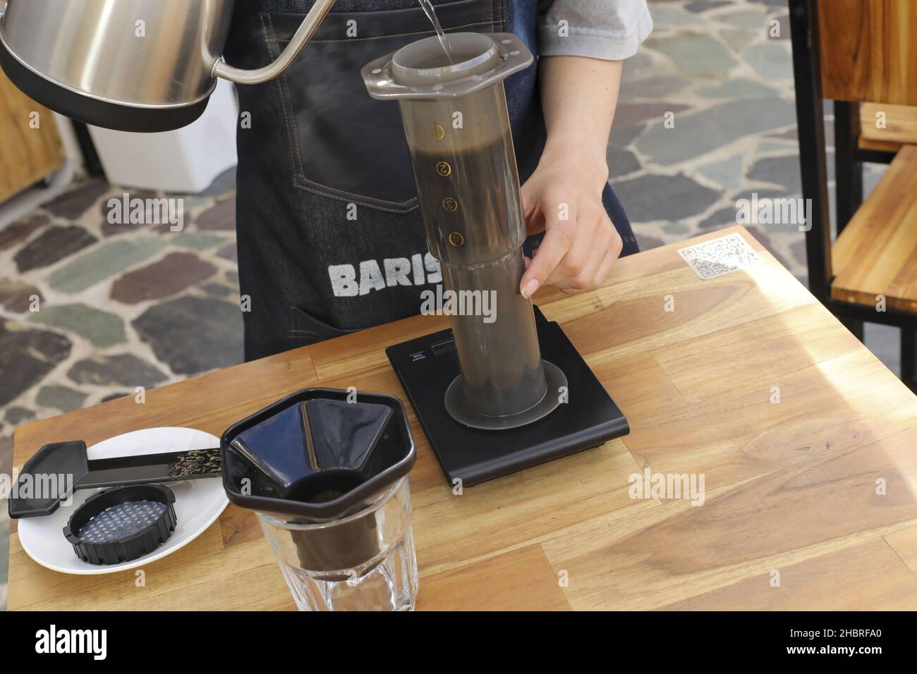 A barista pouring water in a manual coffeemaker on a food weight scale ...