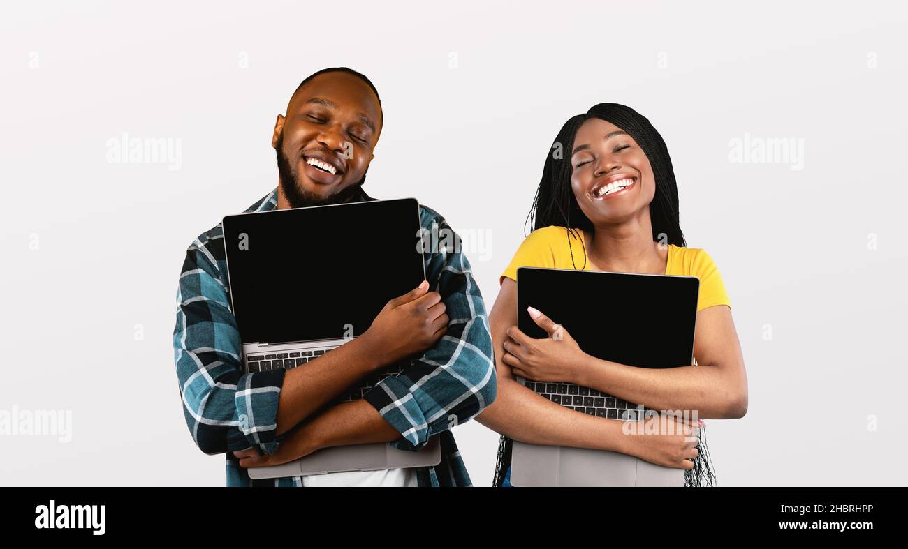 Technology Lovers. Happy black man and woman hugging laptops with blank ...
