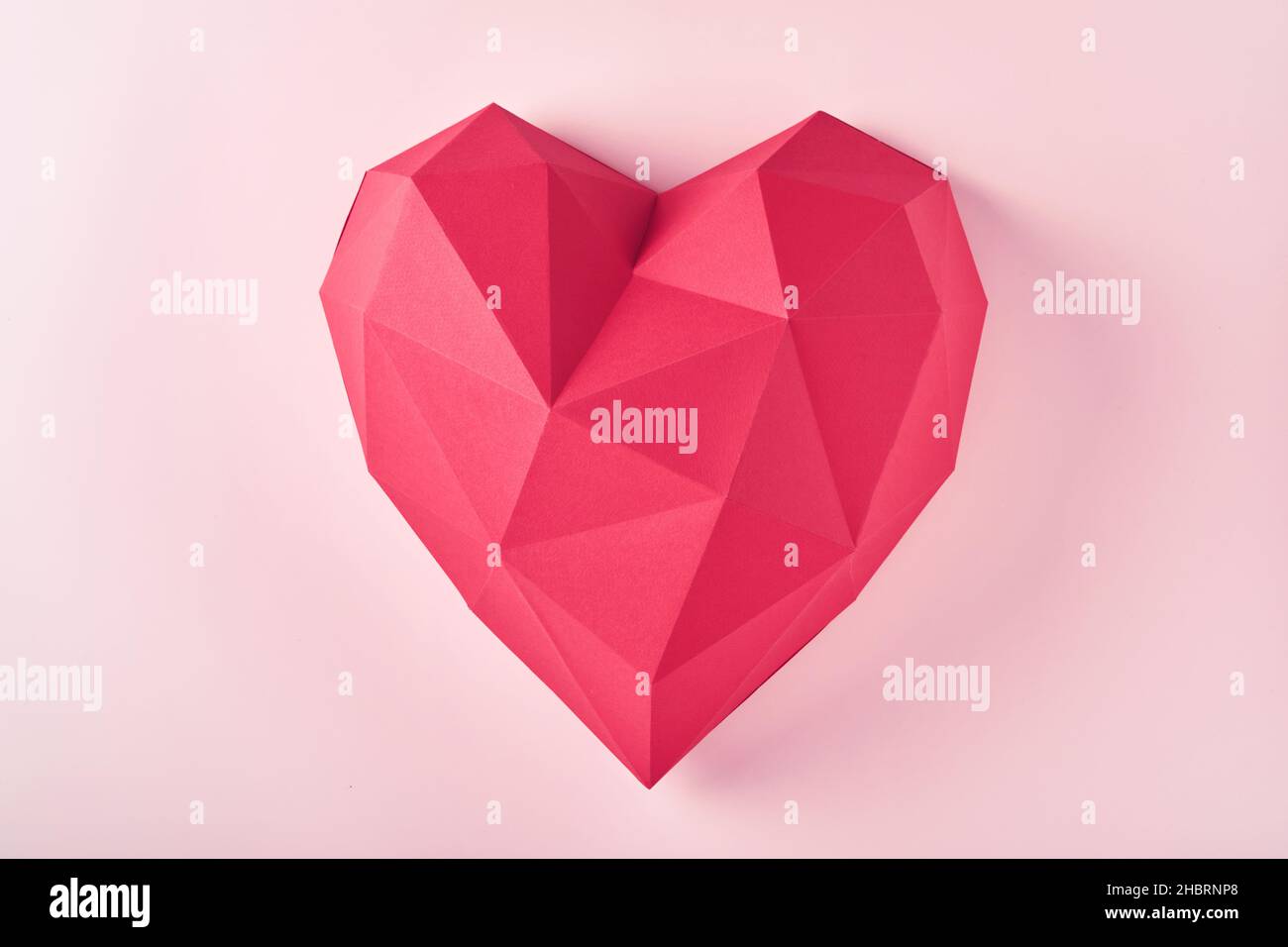 Female hands holding red polygonal paper heart shape on pink background ...