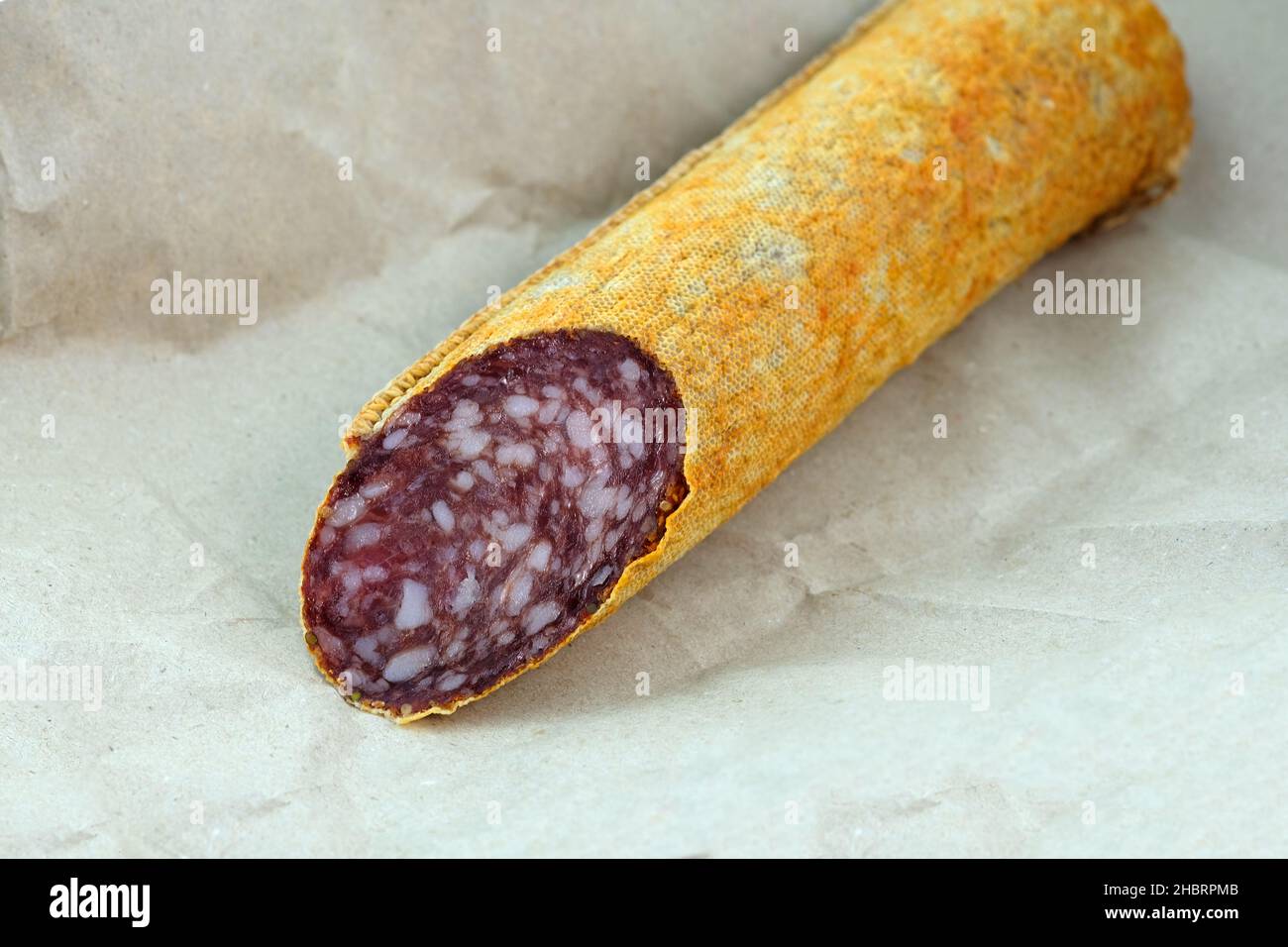 Dry-cured sausage in a fabric casing on craft paper. Stick of smoked ...